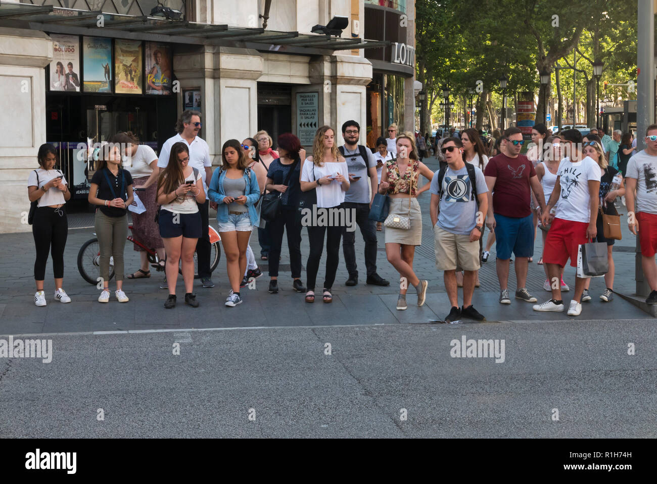 A group of people standing on the pavement waiting to cross the road ...