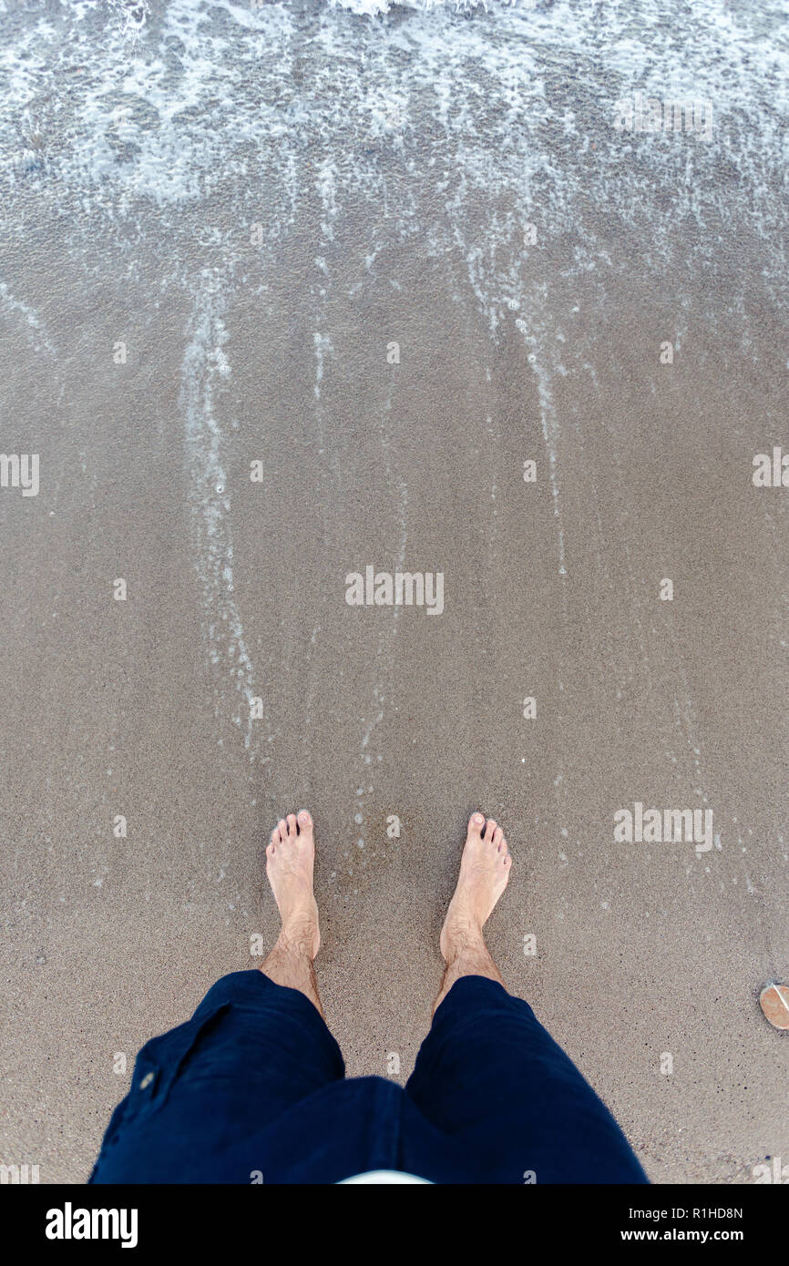 Blue waves in the sand with male feet Stock Photo - Alamy