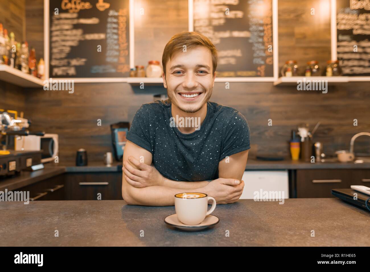 Portrait of young smiling male barista with prepared drink with arms ...