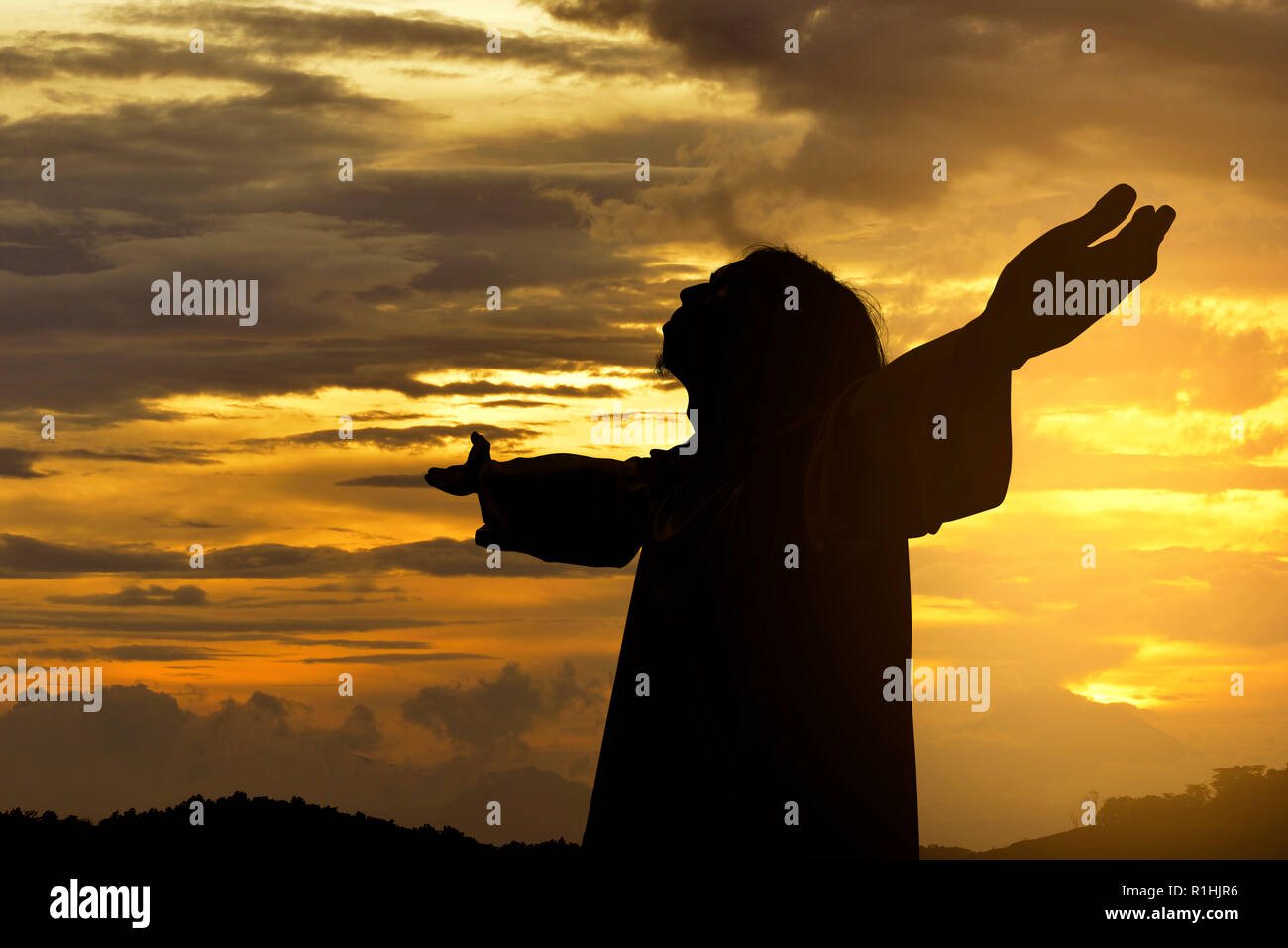 Silhouette of Jesus christ standing with raised arms at sunset ...