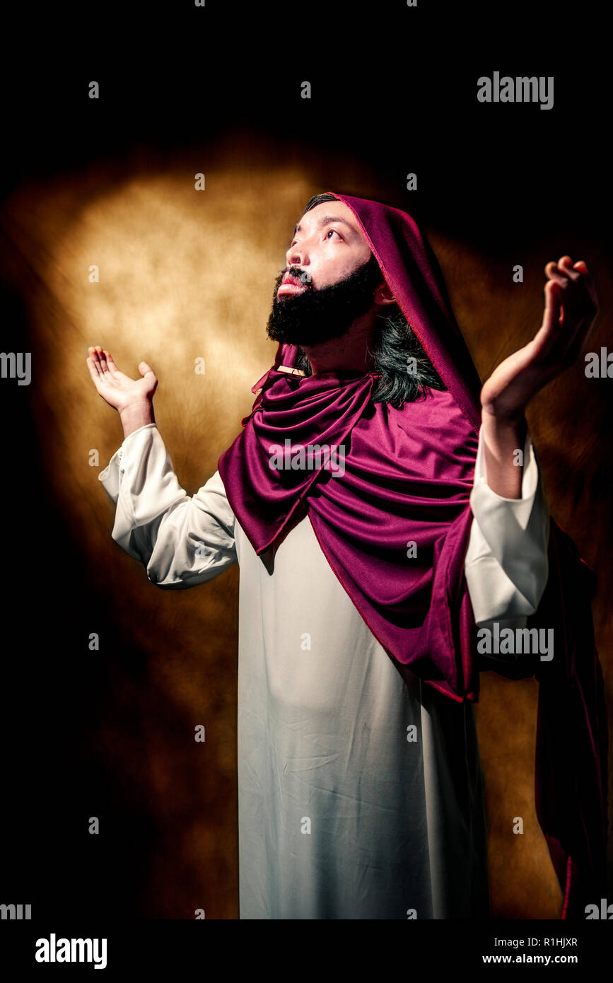Jesus christ raised arms with open palm praying over dark background ...
