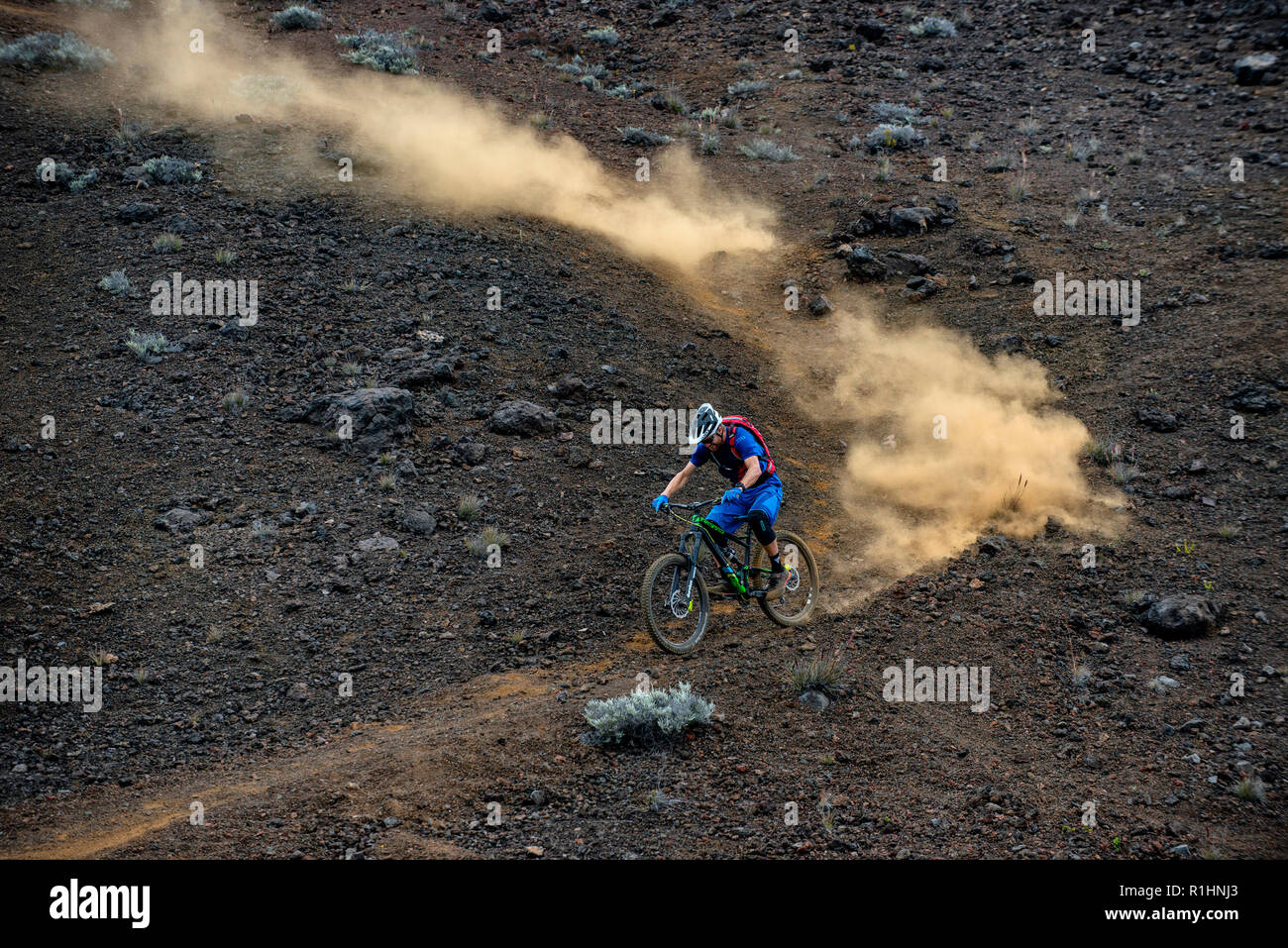A man rides a mountain bike on volcanic terrain near la Piton de la ...