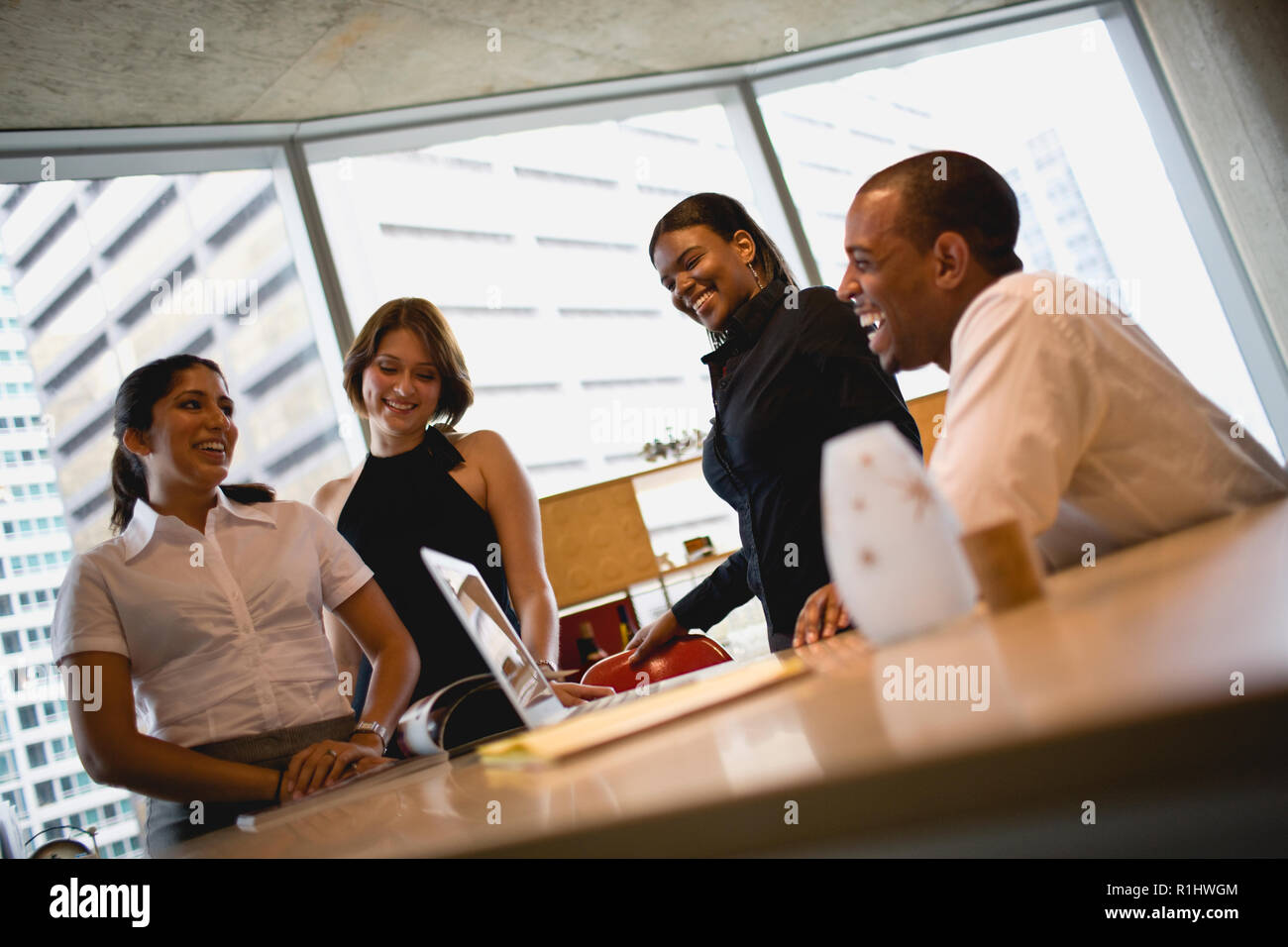 Four young business colleagues laughing while standing inside an office ...