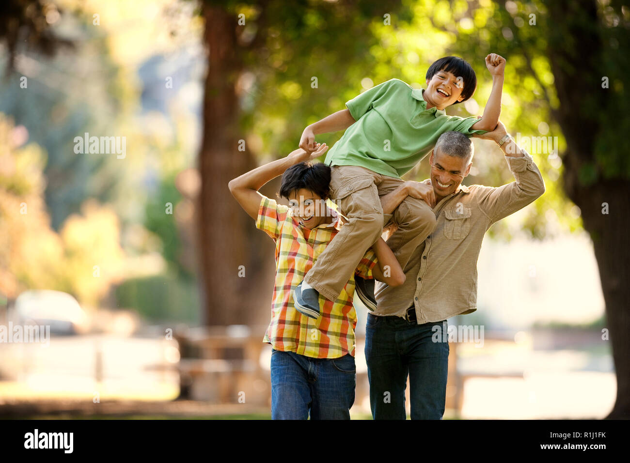 Smiling mid adult man and teenage son playfully carrying a young boy on ...