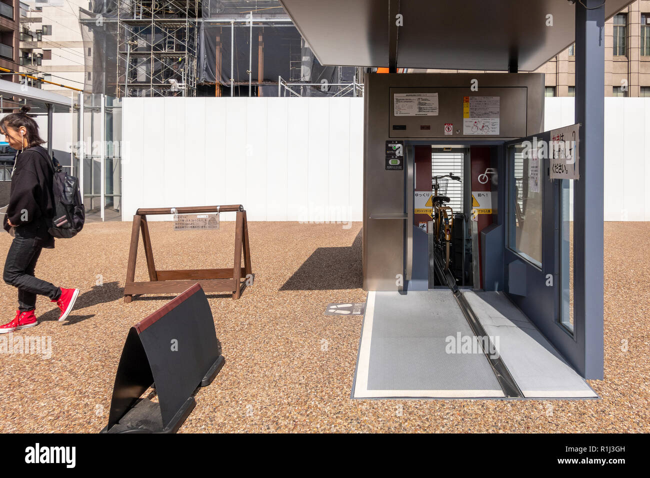 Girl parking her bike in a Giken Eco Cycle automated underground bicycle parking in front of ...