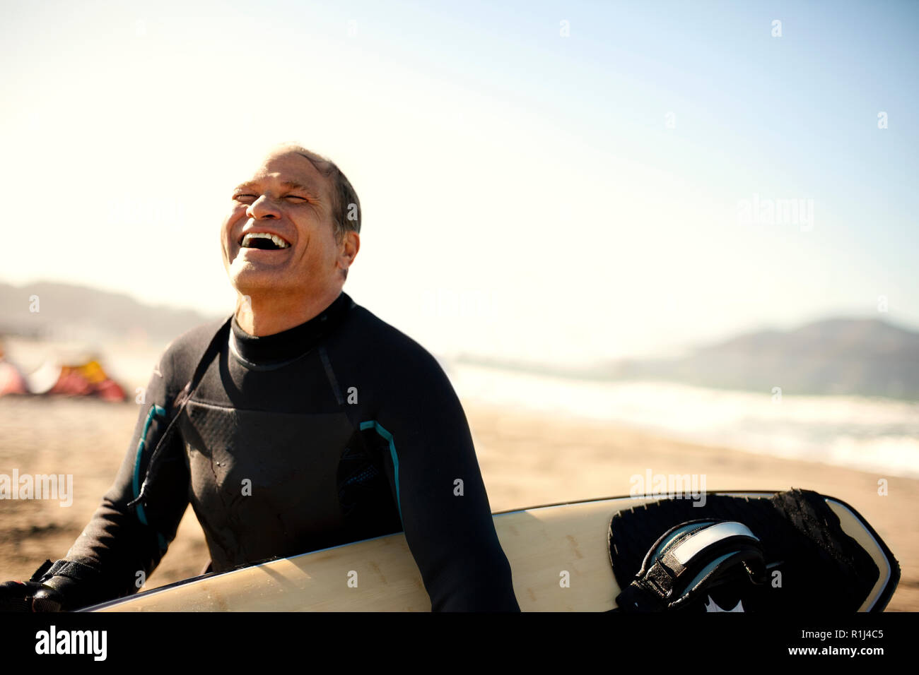 Mid adult man laughing while carrying a surfboard Stock Photo - Alamy
