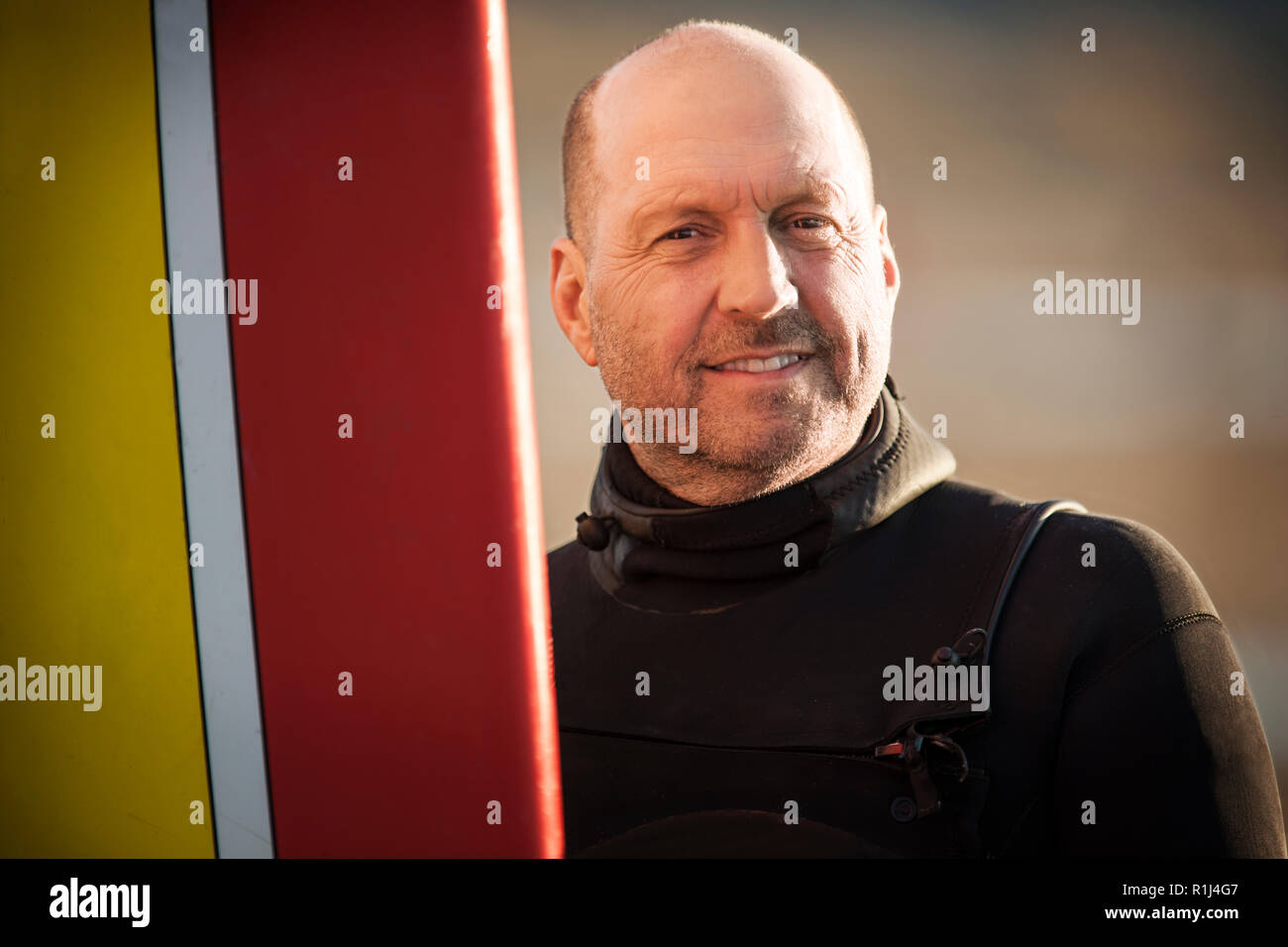 Portrait of a smiling mid adult man standing with his surfboard in the ...