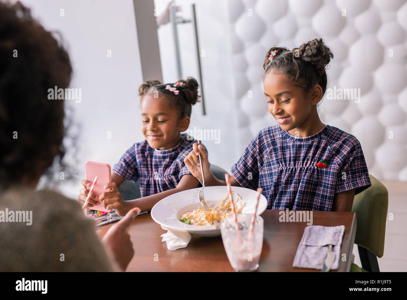 Two daughters feeling excited while eating in cafeteria with mother ...
