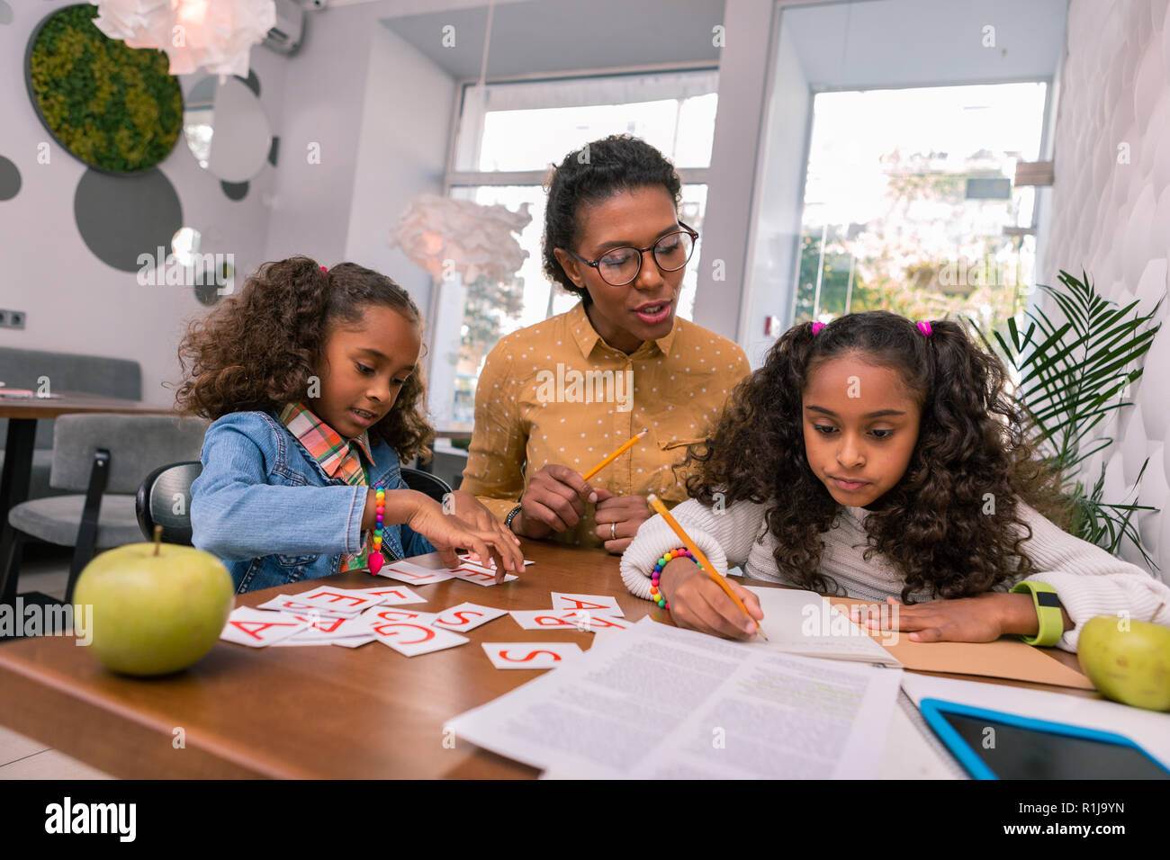 Helpful smart nursery teacher wearing glasses teaching two girls ...