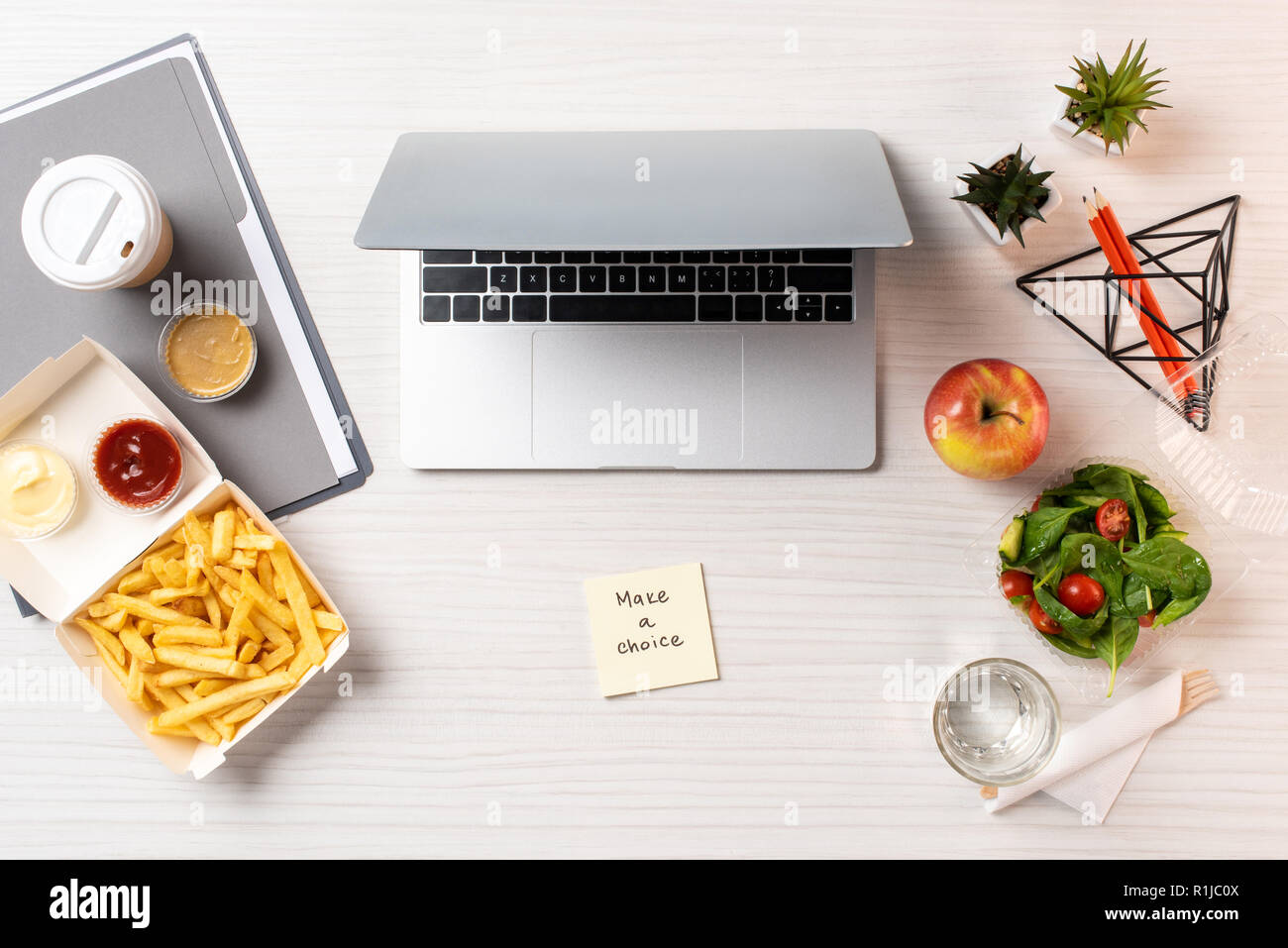 top view of laptop, paper with inscription make a choice and junk food ...