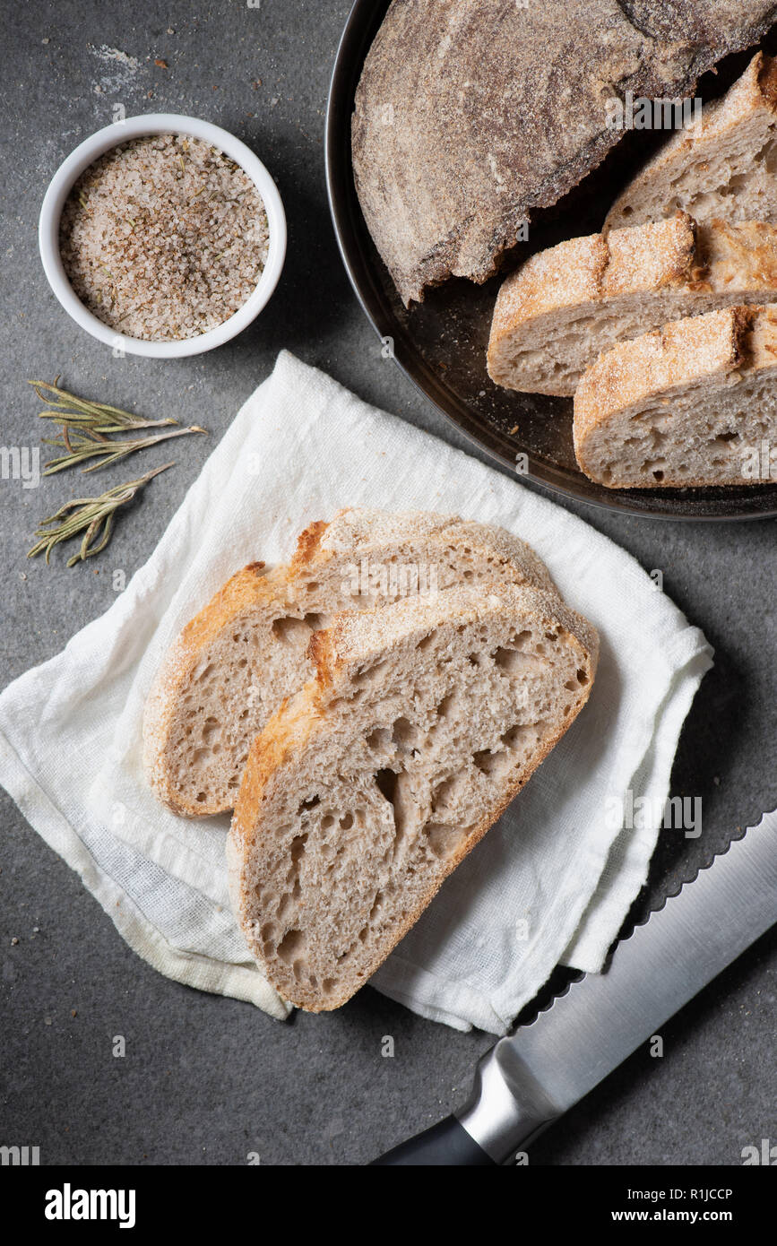 flat lay with cut loaf of bread, knife and white linen on grey tabletop ...