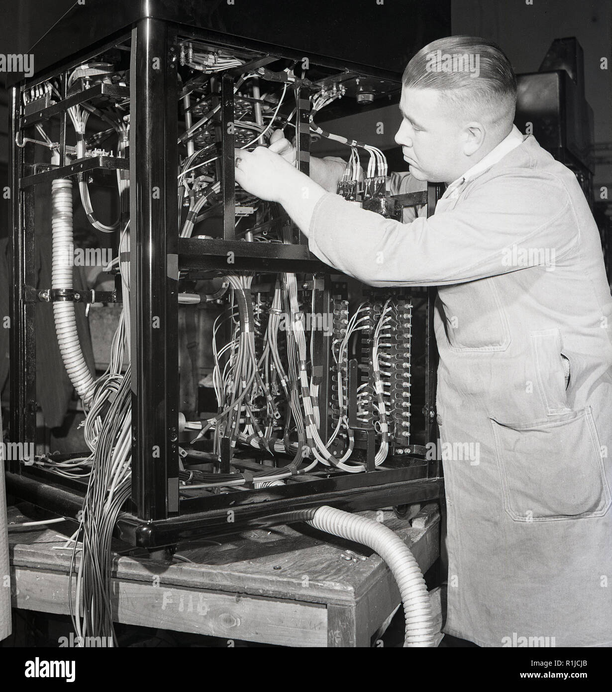 1950s, historical, a male technician in overalls working on a piece of ...