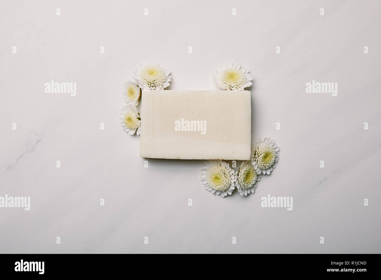 top view of handmade soap piece with daisies on white marble surface ...