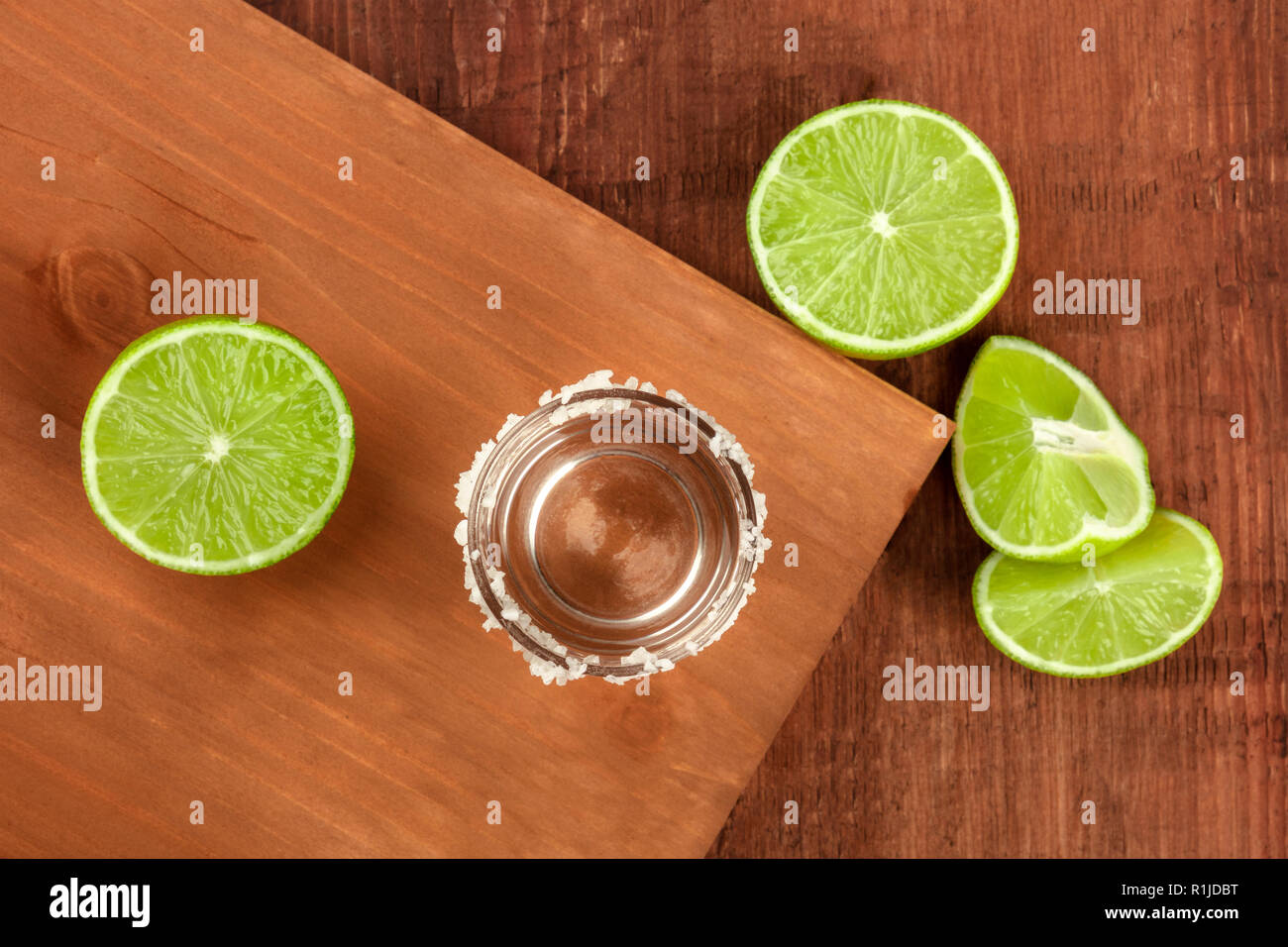 A tequila shot with lime wedges, shot from the top on dark rustic ...