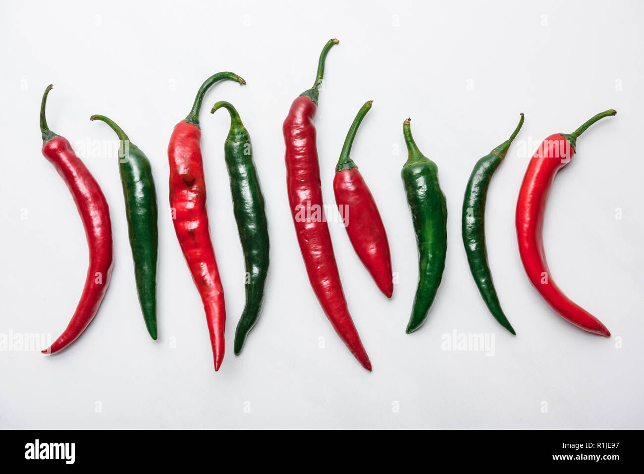 top view of red and green chili peppers in row on white marble tabletop ...