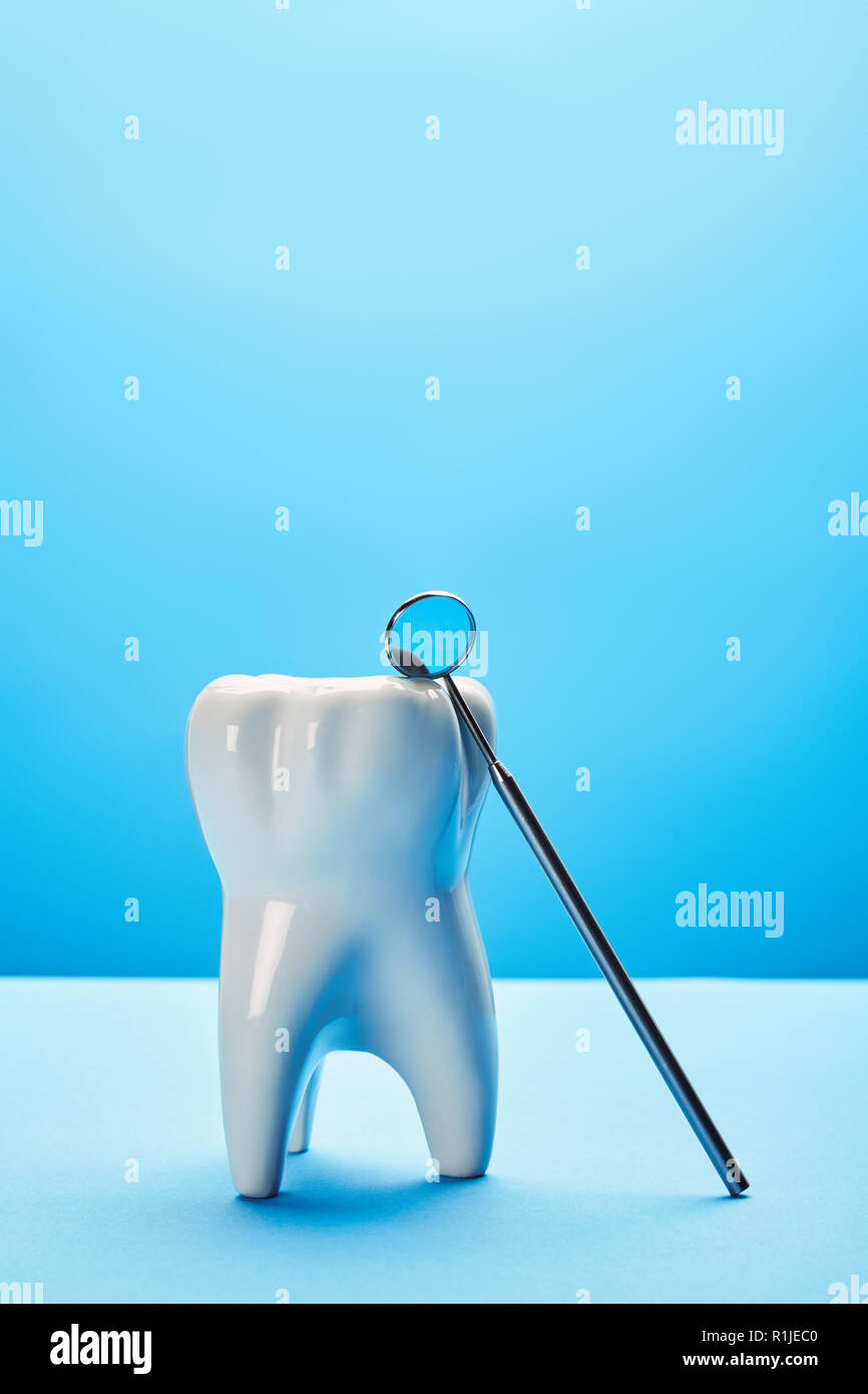 close up view of tooth model and dental mouth mirror on blue backdrop ...