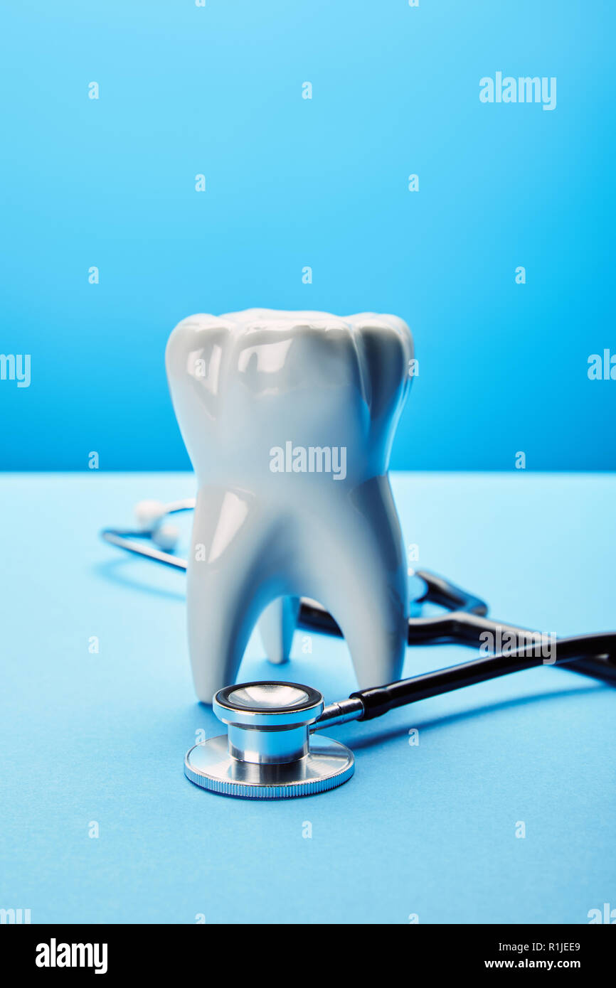 close up view of white tooth model and stethoscope on blue backdrop ...