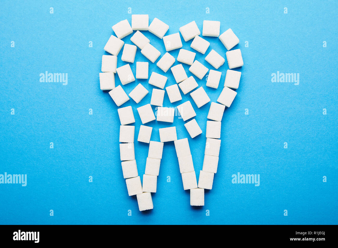 top view of white sugar cubes arranged in tooth sign on blue background ...