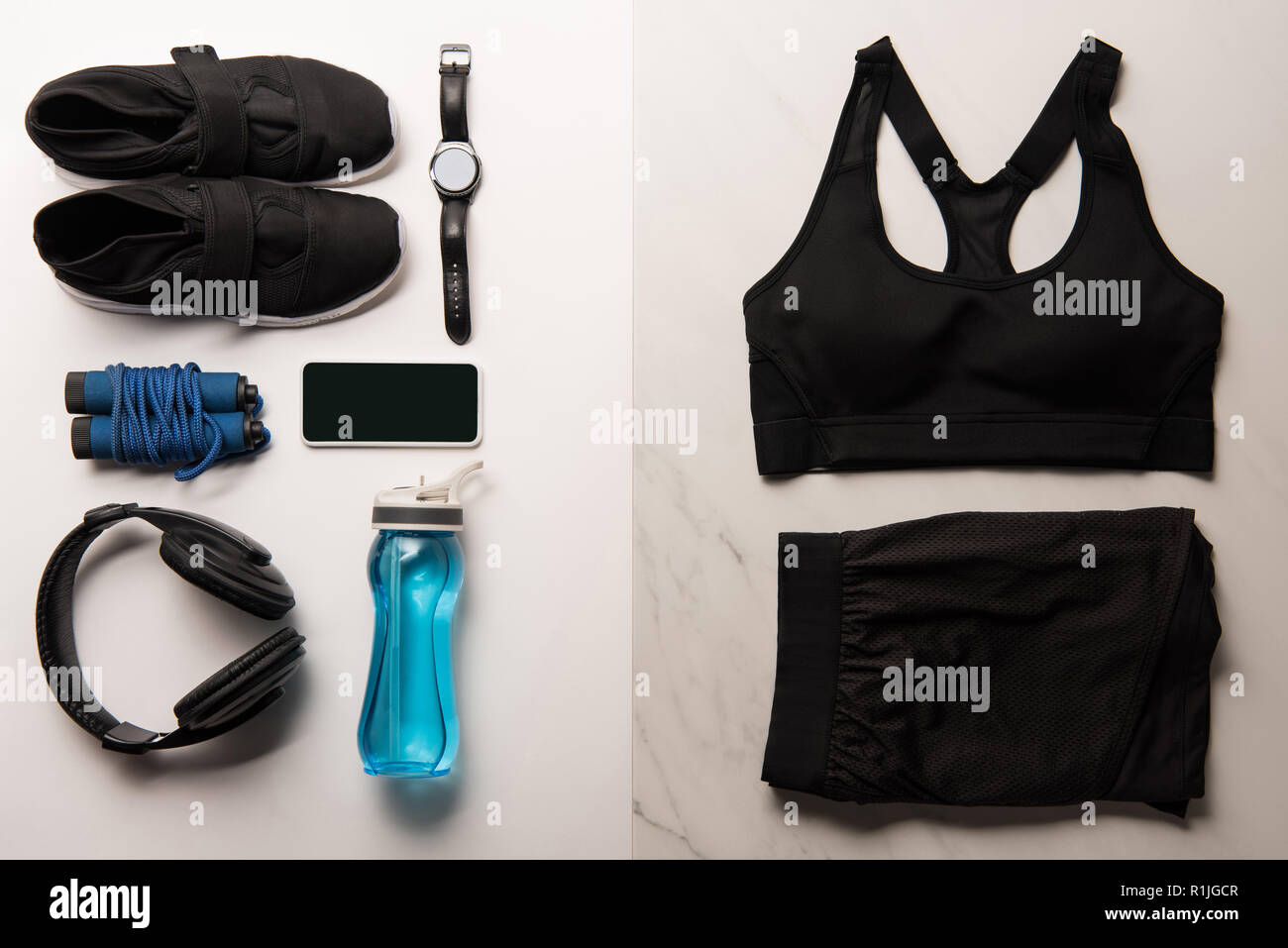 top view of black sportswear with arranged gym equipment on white and ...
