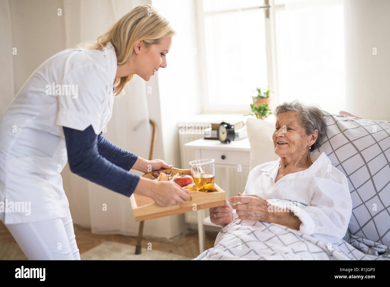 A health visitor bringing breakfast to a sick senior woman lying in bed ...