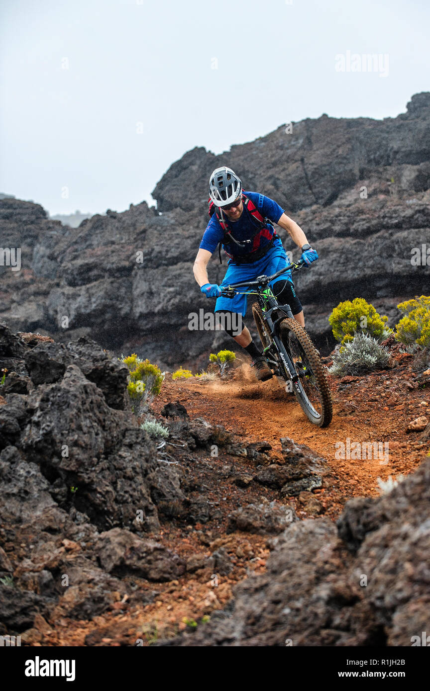 A man rides a mountain bike on volcanic terrain near la Piton de la ...