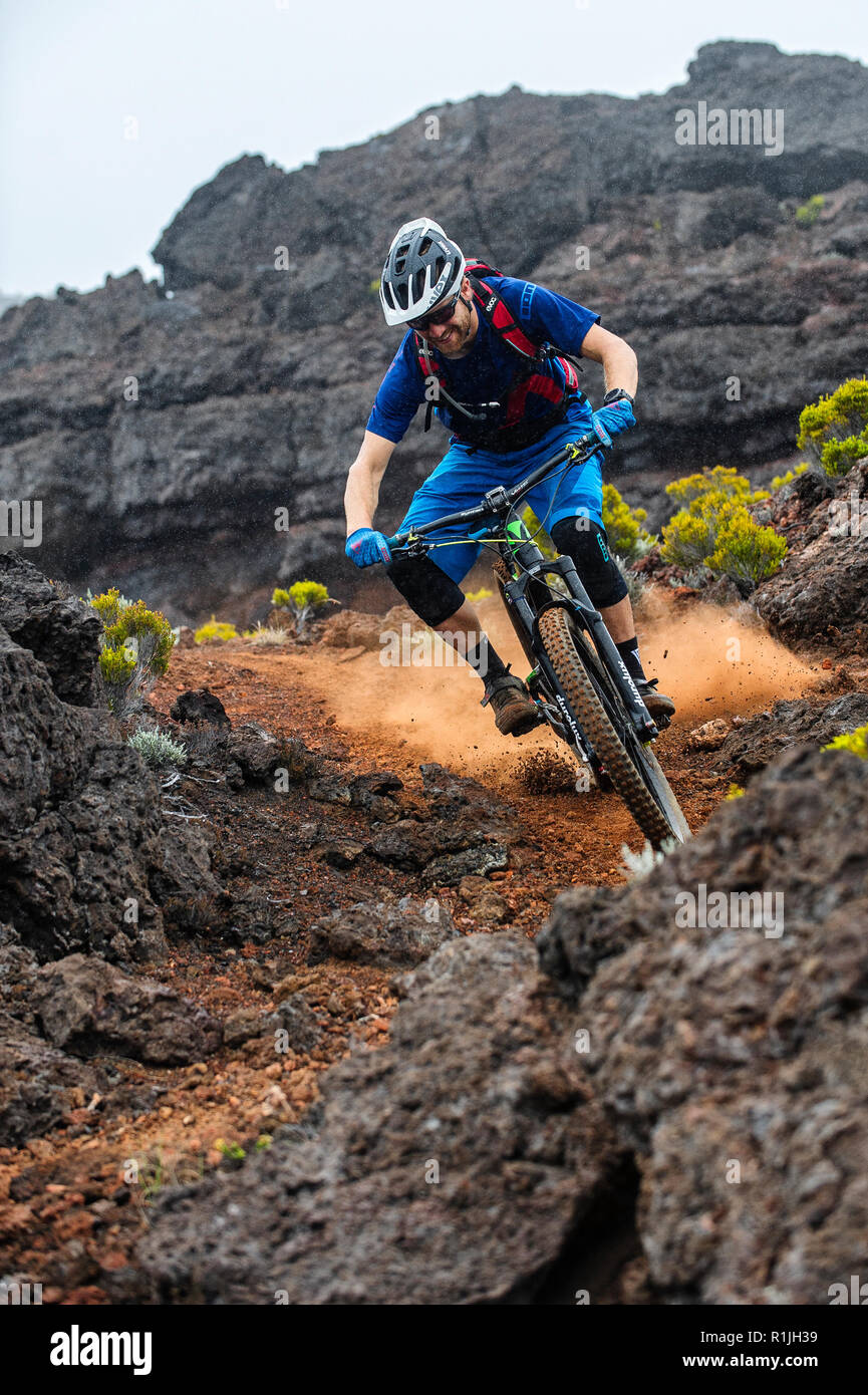 A man rides a mountain bike on volcanic terrain near la Piton de la ...