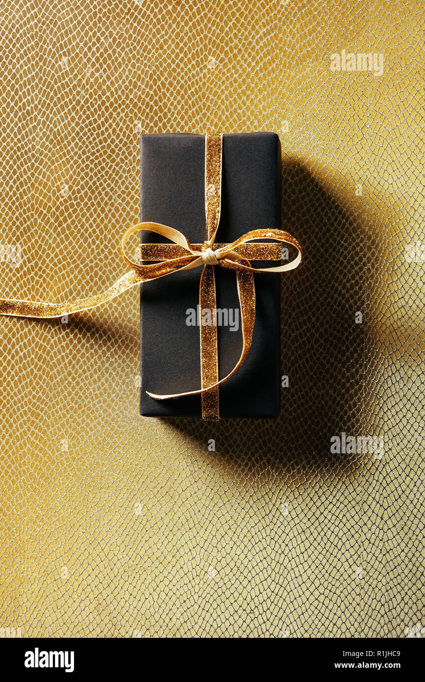 top view of wrapped gift box with golden ribbon on golden background ...