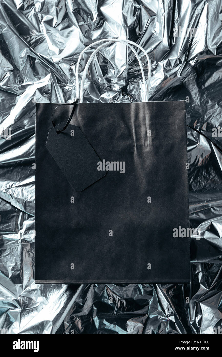 top view of black paper bag with blank price tag on silver wrapping ...