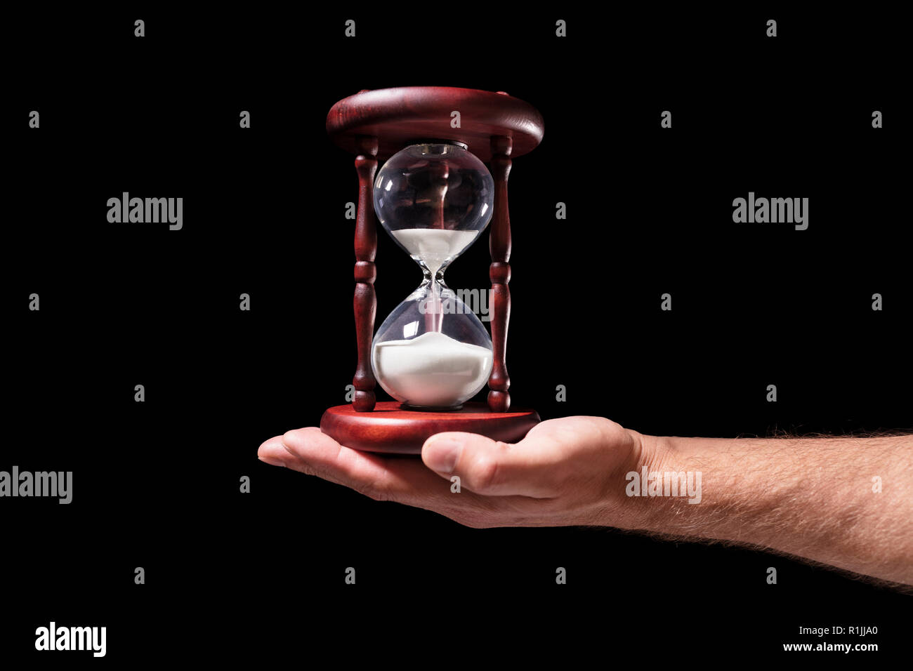 Hand holding hourglass over black background concept for time passing ...