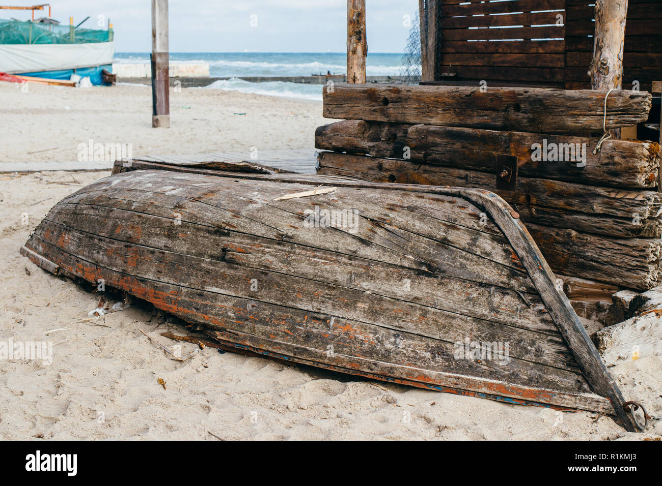 Old rusty wooden fishing boat laying overturned on sand coast near sea ...
