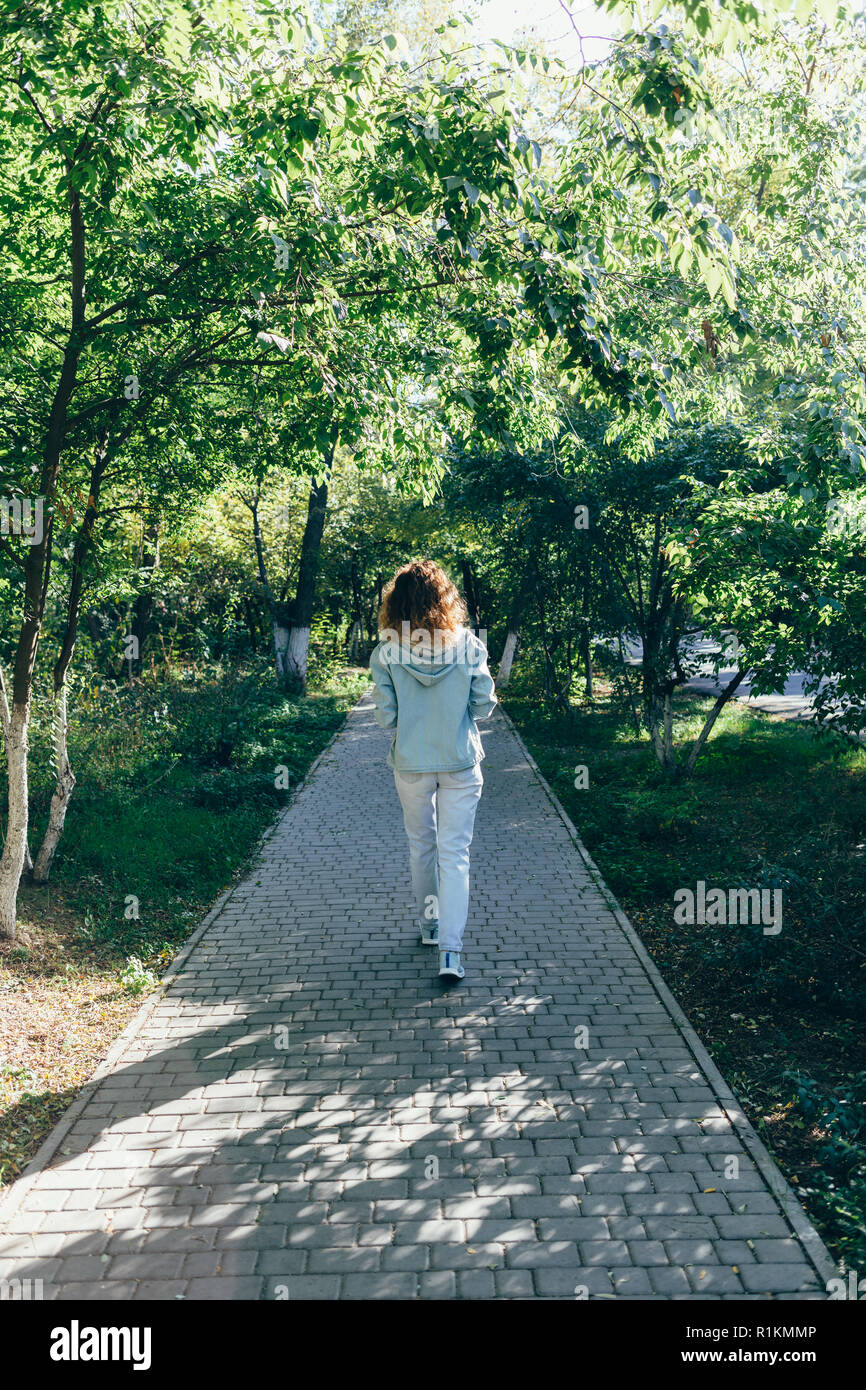 Young woman walking away on path in green park at sunny day. Full ...