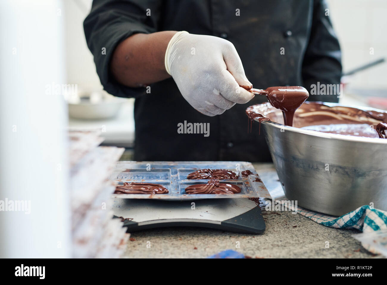 Confectionary making factory worker putting melted chocolate into molds ...