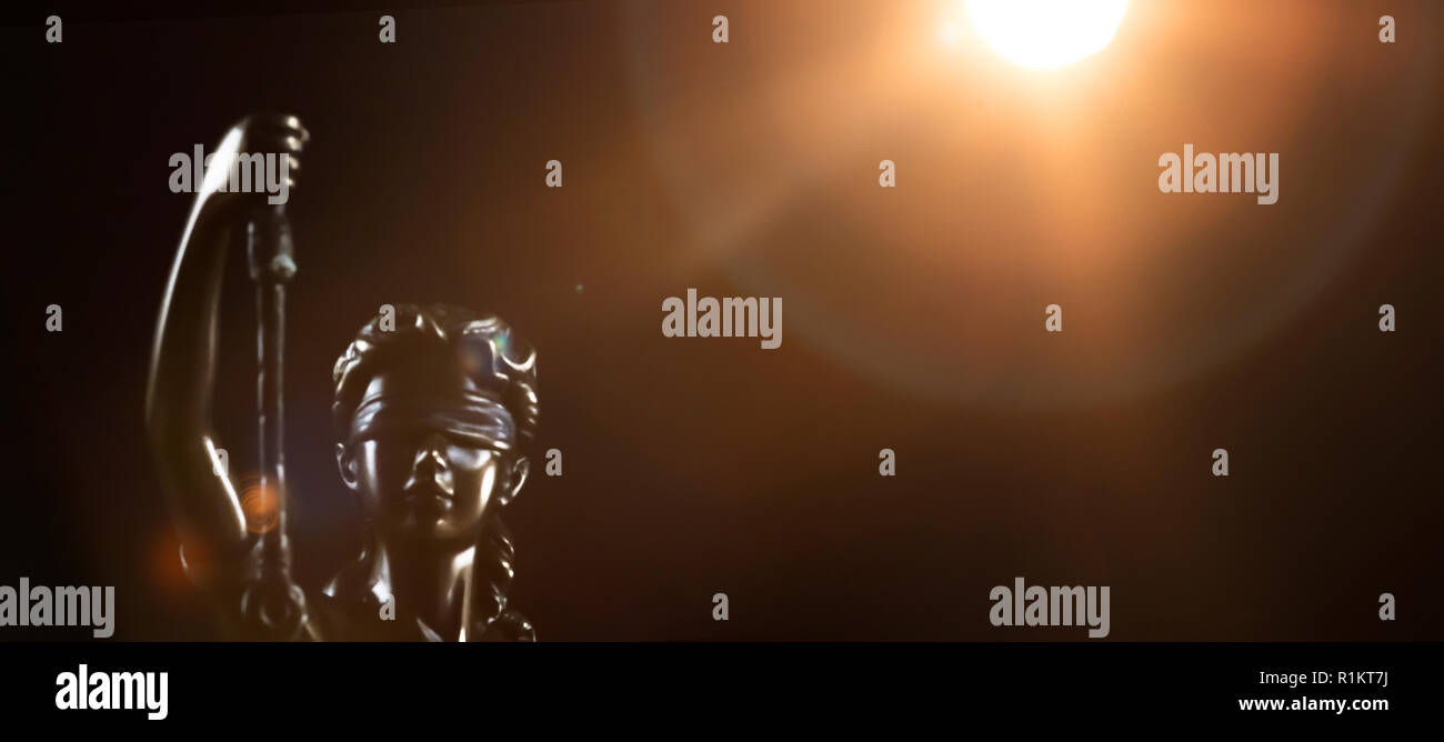 A golden statue of lady justice stands in black surroundings. The sun ...