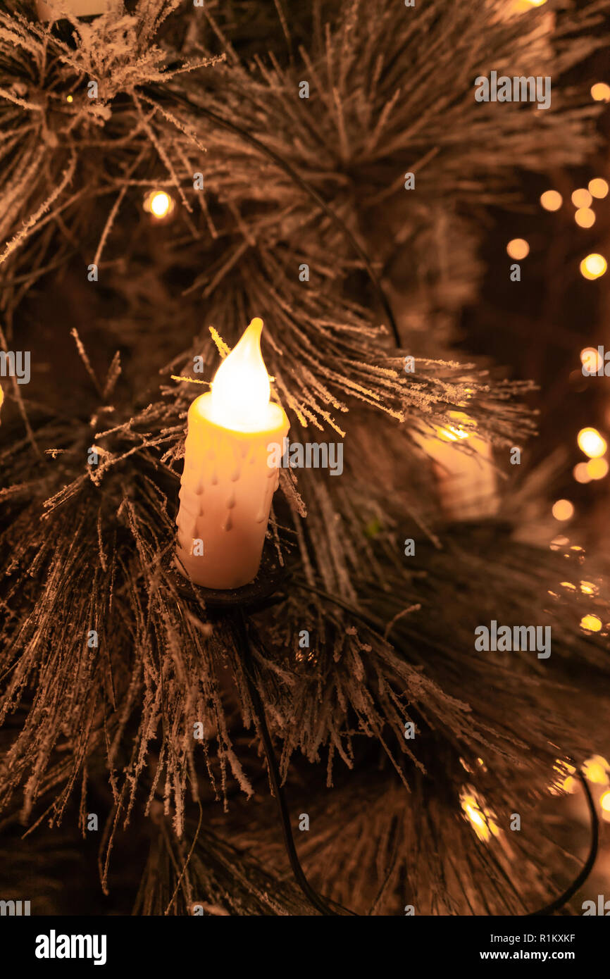 Traditional candles on flocked Christmas tree with glowing lights ...