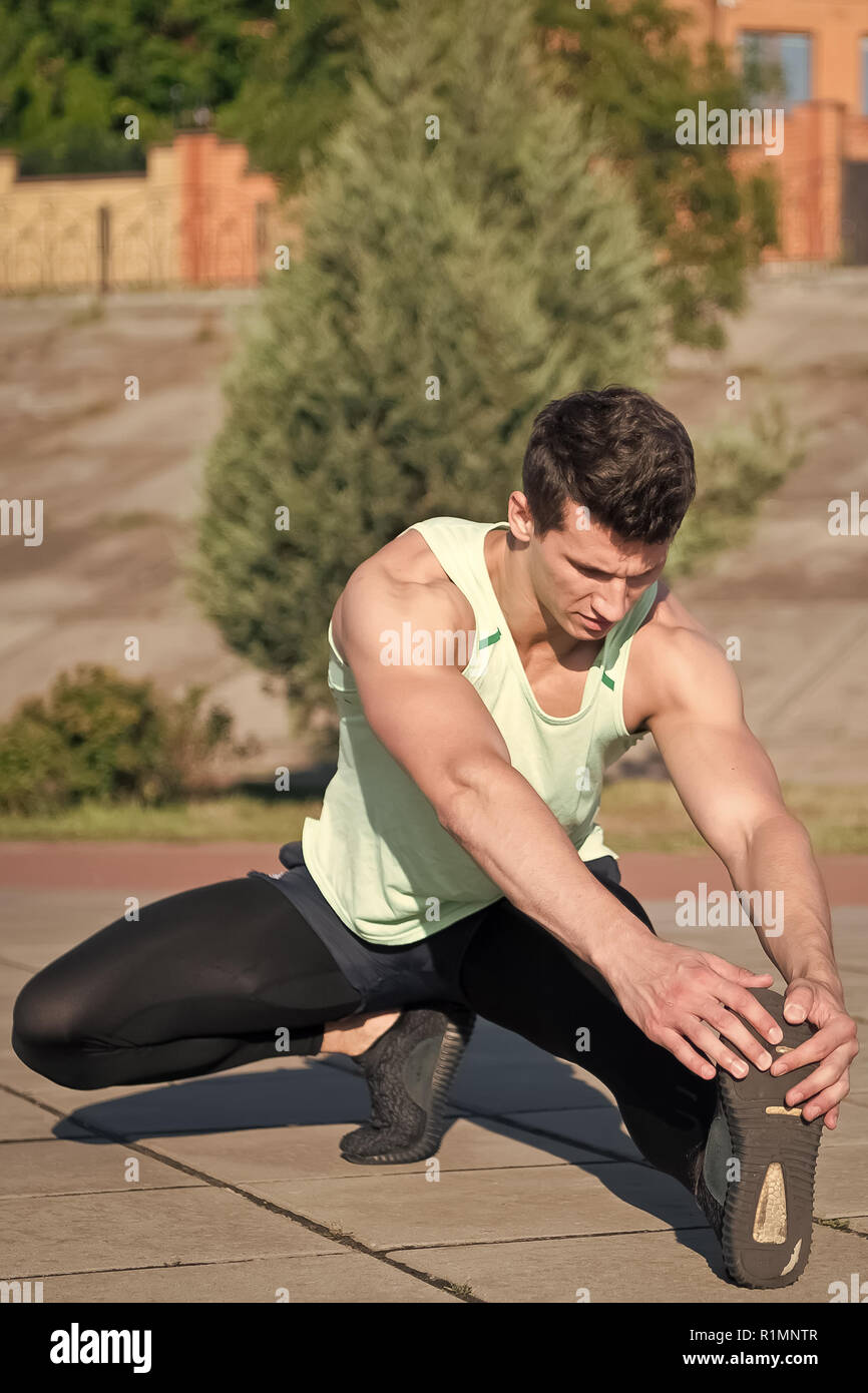 Fit macho in track suit on urban landscape. Man stretching and warming ...