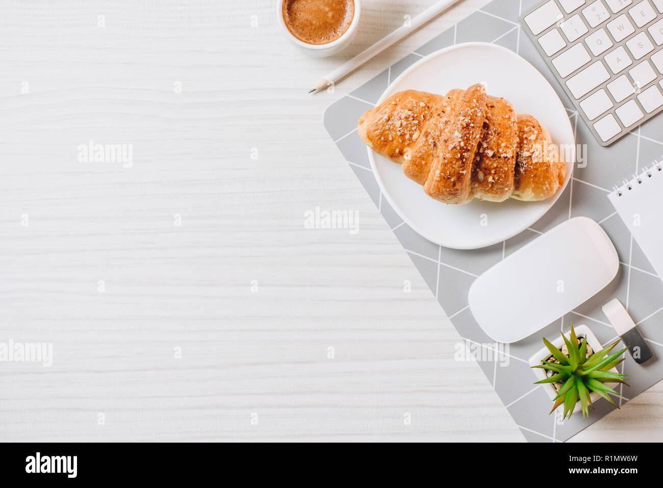 top view of workplace with arranged croissant, coffee cup and computer ...