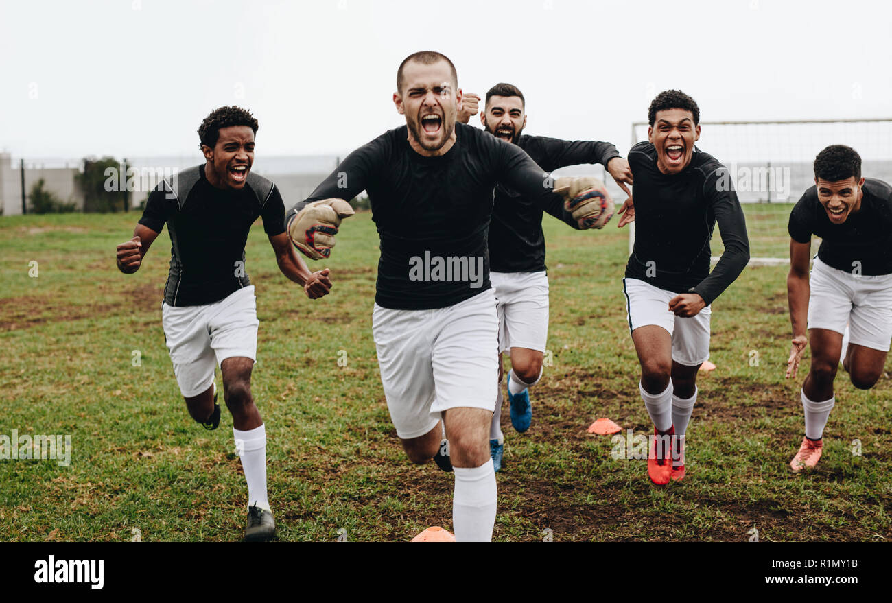 Group of football players running on field shouting in joy after ...