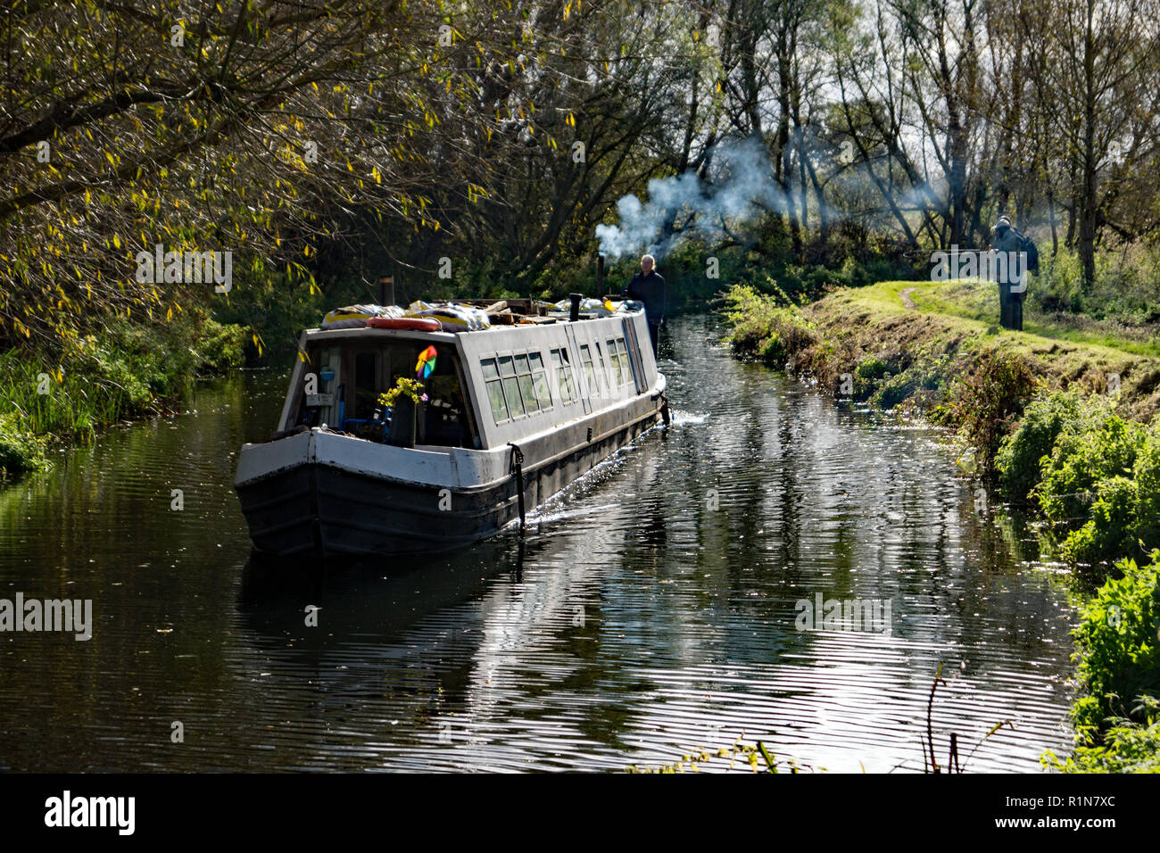 A canal, or narrow, boat passing two fishermen angling on the banks of ...
