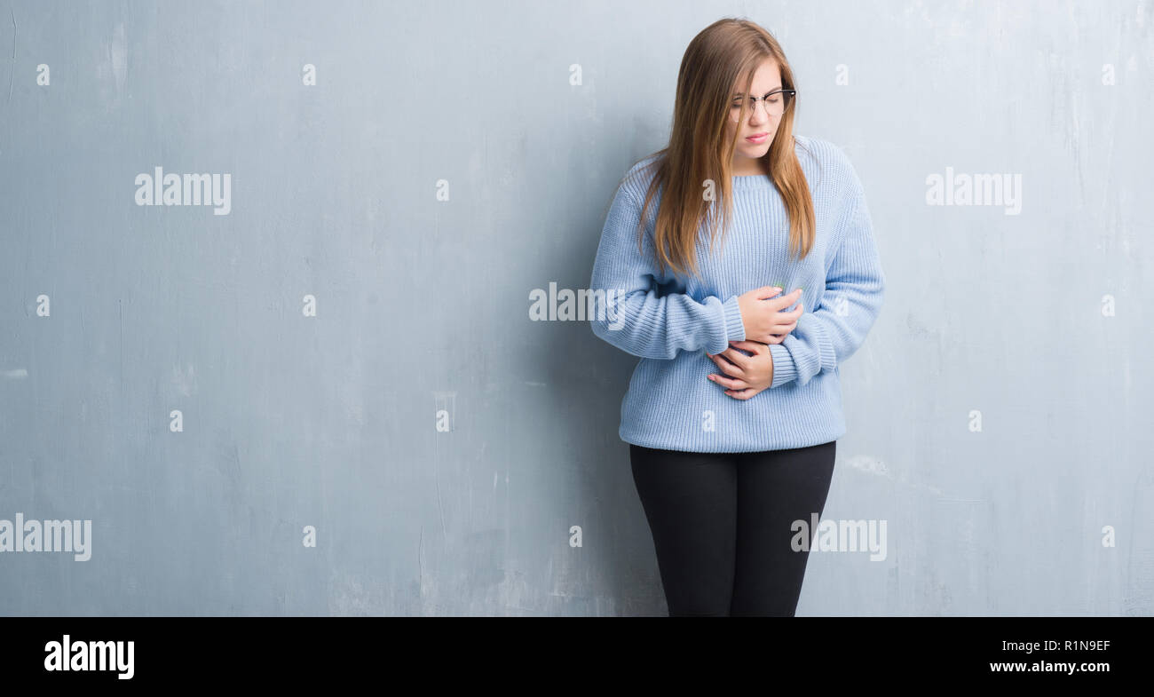 Young adult woman over grey grunge wall wearing glasses with hand on ...