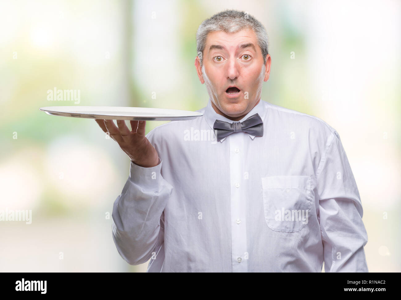 Handsome senior waiter man holding silver tray over isolated background ...