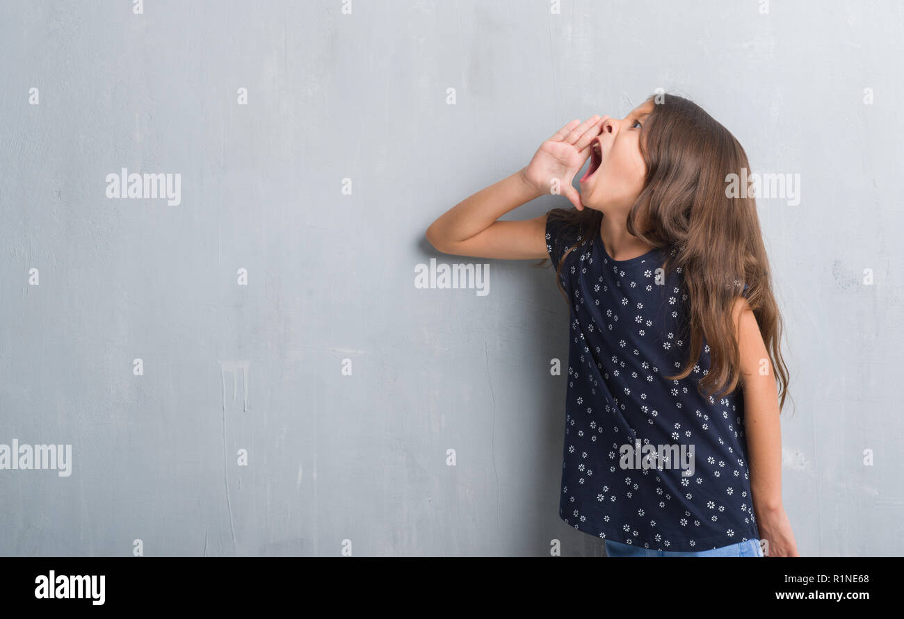 Young hispanic kid over grunge grey wall shouting and screaming loud to ...
