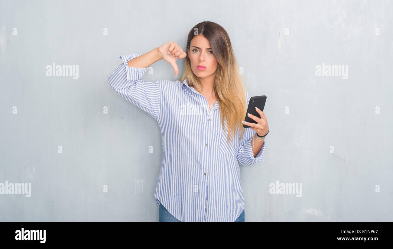 Young adult woman over grey grunge wall looking at smartphone texting a ...