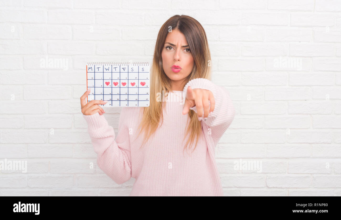 Young adult woman over white brick wall holding period calendar ...