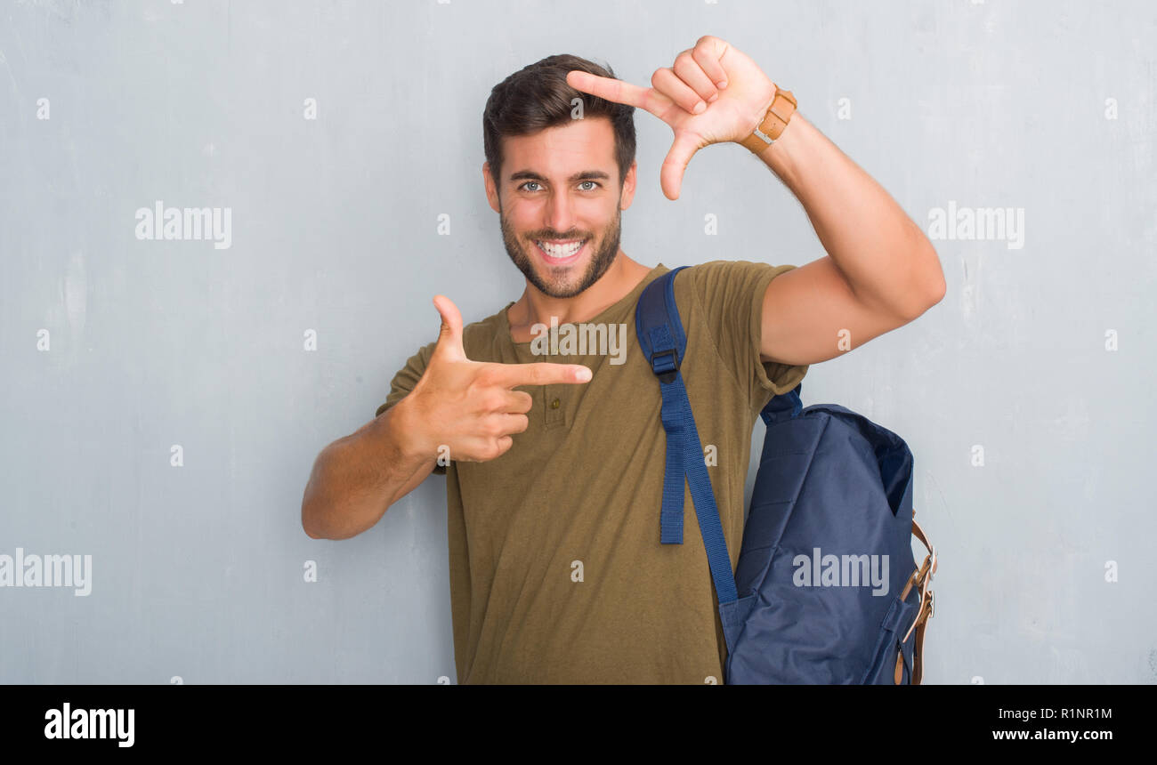 Handsome tourist young man over grey grunge wall wearing backpack ...