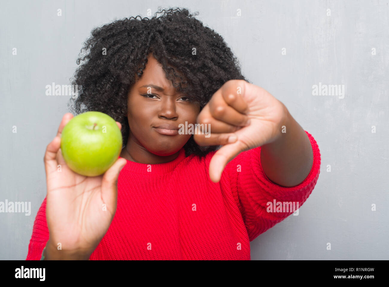 Young african american woman over grey grunge wall eating green apple ...
