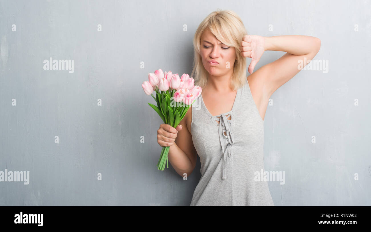 Caucasian adult woman over grey grunge wall holding pink flowers with ...