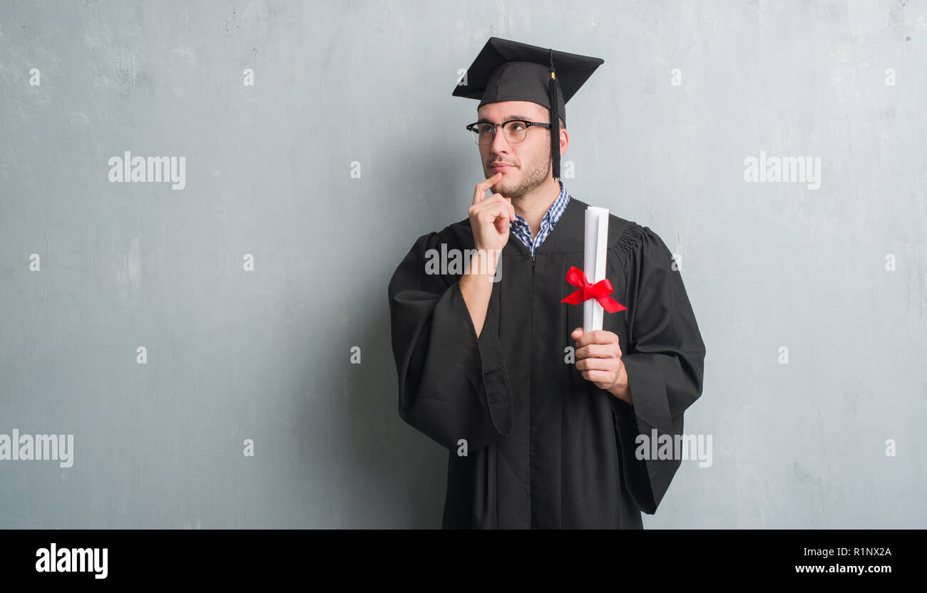 Young caucasian man over grey grunge wall wearing graduate uniform ...