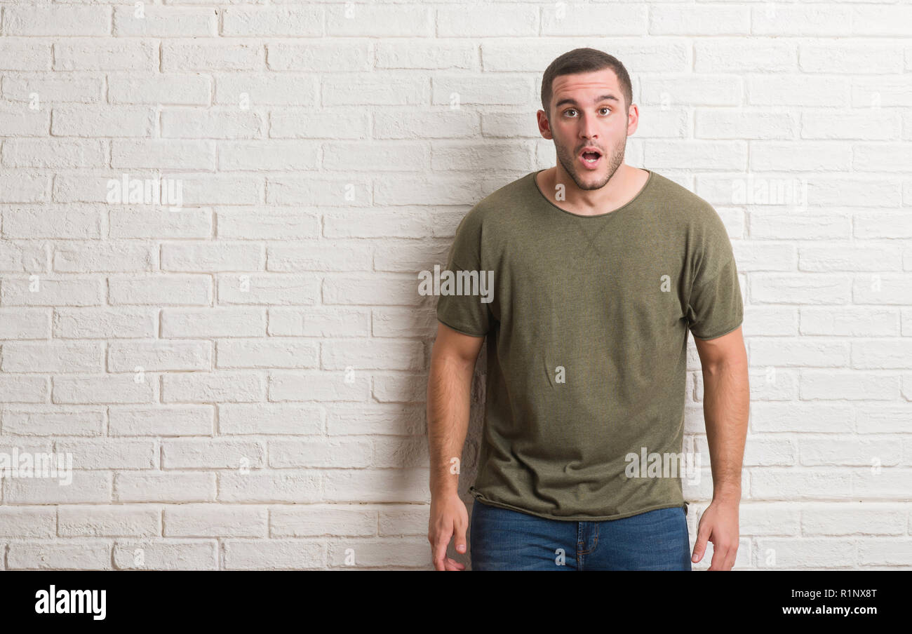 Young caucasian man standing over white brick wall afraid and shocked ...
