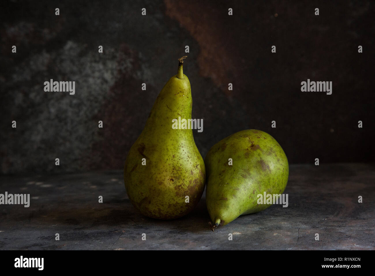 Two whole pears with green and brown skins on a grey textured ...