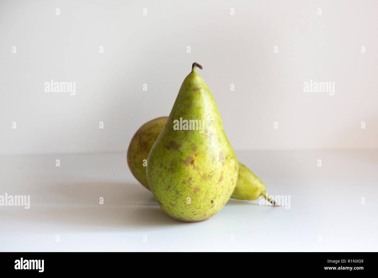 Two green pears sitting on a white background in soft lighting with ...